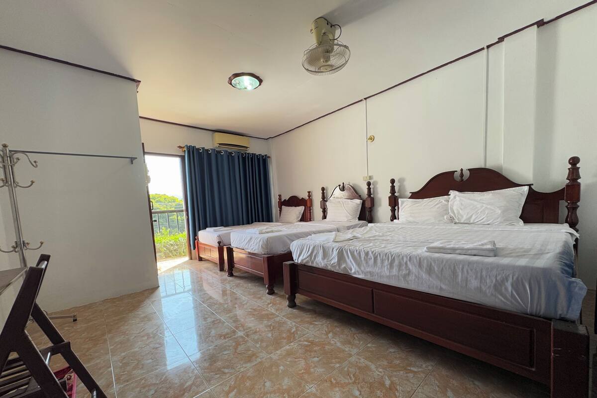 Quarto de hotel com duas camas de solteiro, ventilador de teto e varanda com cortinas.
