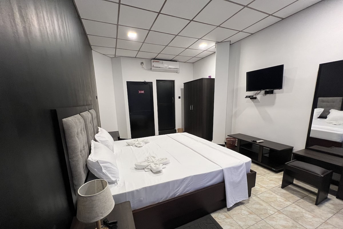 Quarto de hotel moderno com uma cama grande, televisão de tela plana na parede, escrivaninha e uma cadeira.