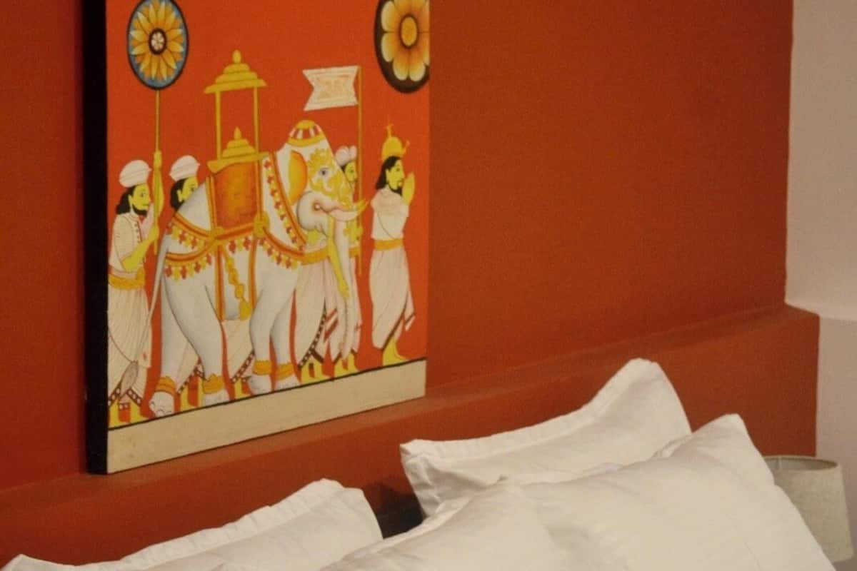 Quarto de hotel com cama, almofadas brancas e parede com uma pintura colorida.
