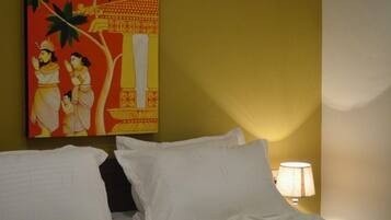 Quarto de hotel com cama, almofadas brancas, abajur e um quadro na parede.