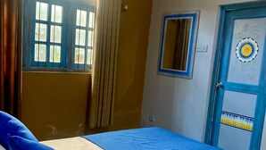 Quarto com cama, janela com cortinas, porta com painel decorativo e espelho fixado na parede.