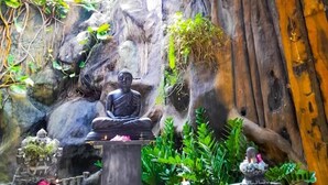 Um jardim interior tranquilo com uma estátua de Buda, pilares de pedra e um telhado de palha.