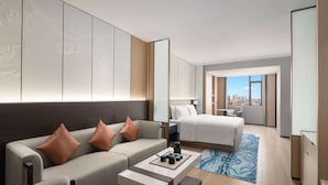 Quarto de hotel moderno com sofá, cama, escrivaninha e vista da cidade.