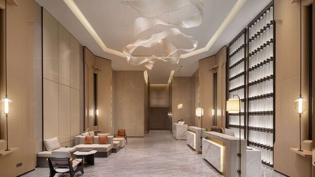 Um saguão de hotel moderno com balcão de recepção, área de estar e um grande candelabro.