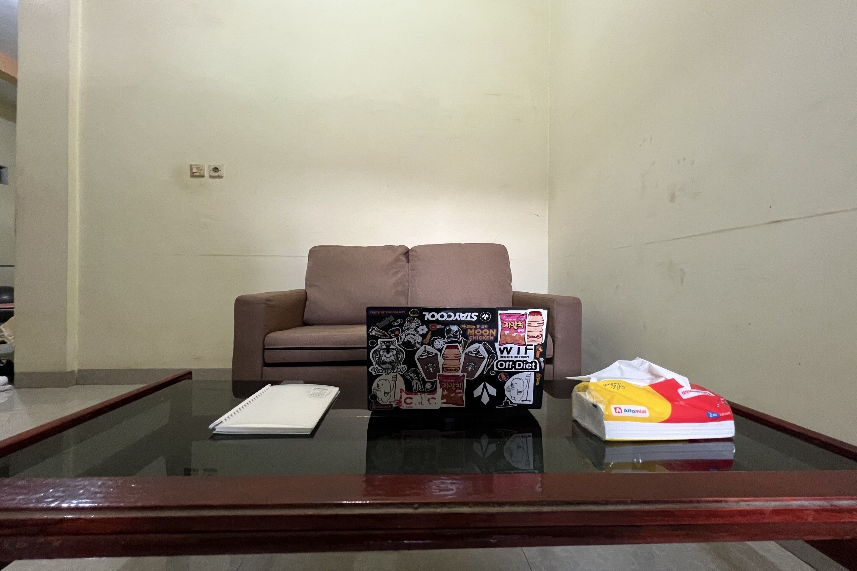 Um quarto com uma mesa de centro de vidro, um sofá marrom e uma caixa de lenços.