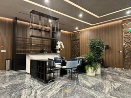Uma área de recepção moderna com piso de mármore, balcão de atendimento, espaço para sentar e plantas decorativas.