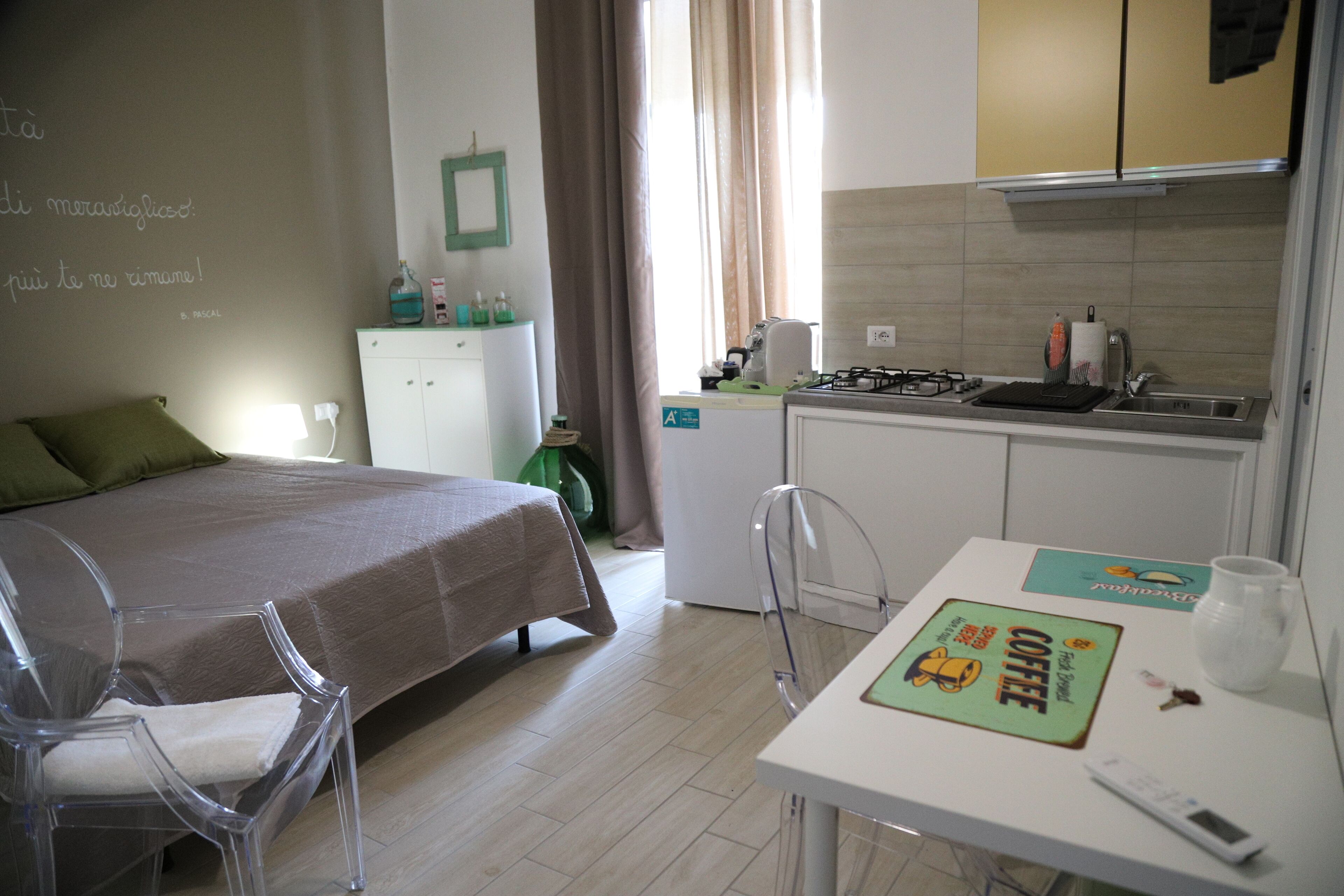 Quarto de hotel compacto com cama, pequeno espaço de cozinha e área de refeições.