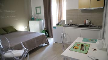 Quarto de hotel compacto com cama, pequeno espaço de cozinha e área de refeições.