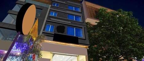 Um hotel de vários andares com design arquitetônico moderno, apresentando um logotipo circular proeminente na fachada e uma entrada visível com portas de vidro.