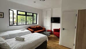Um quarto moderno com uma cama grande, um sofá vermelho, uma mesa pequena e uma TV fixada na parede.