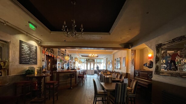 Restaurante com área de bar, mesas e cadeiras de madeira e um lustre.