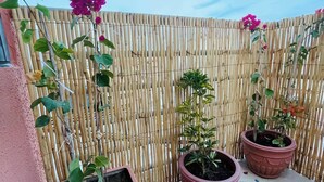 Uma varanda com cerca de bambu, plantas em vasos e uma parede rosa.