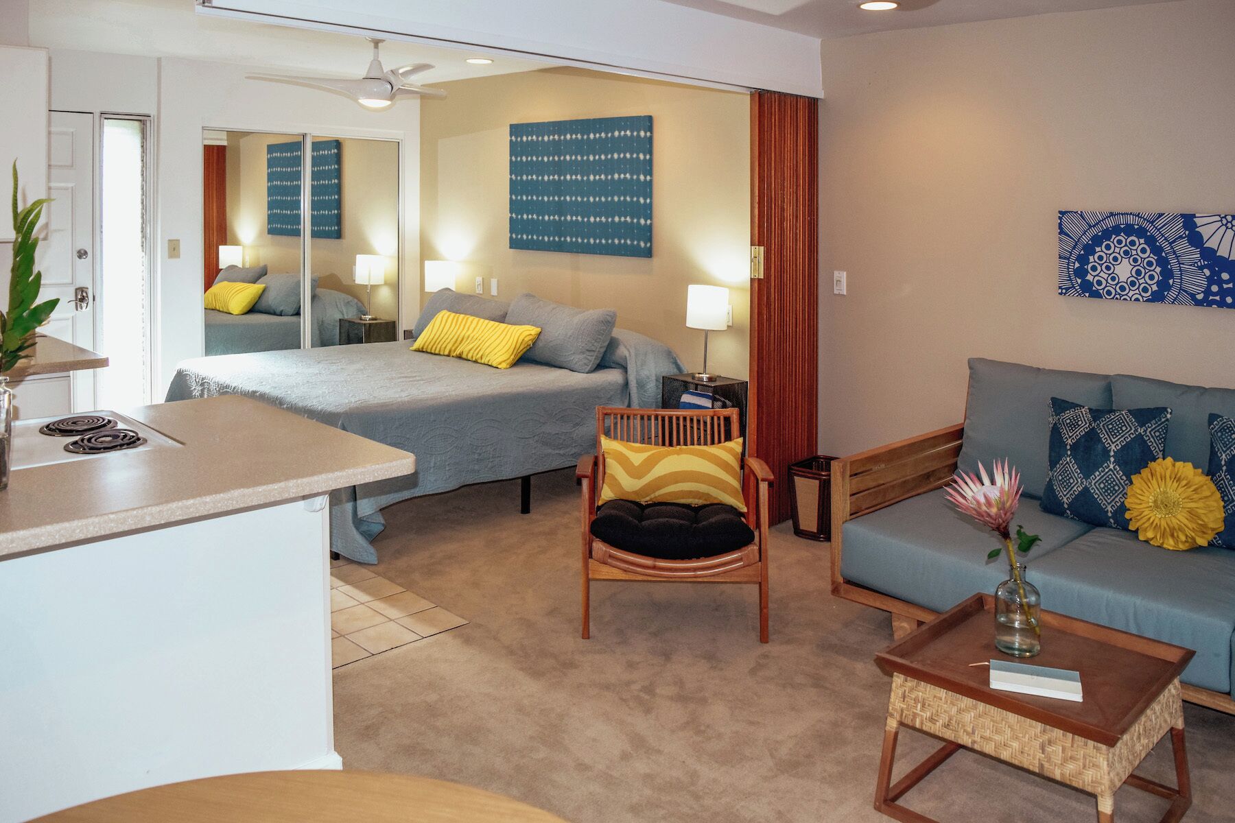 Quarto de hotel com cama, cadeira, sofá, mesinha e cozinha.