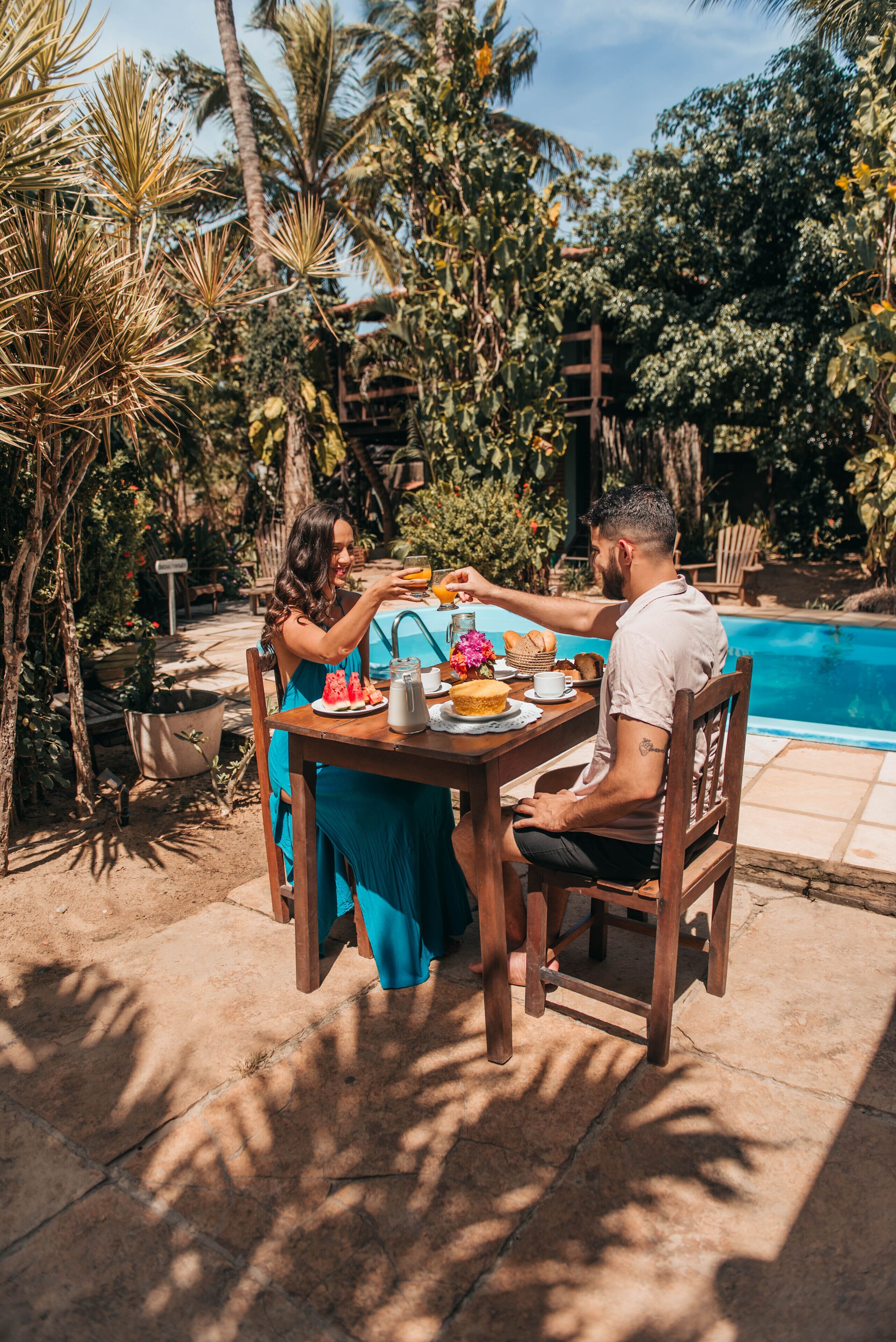 Mesa de jantar com toalha azul, rodeada por cadeiras, e uma piscina ao fundo.