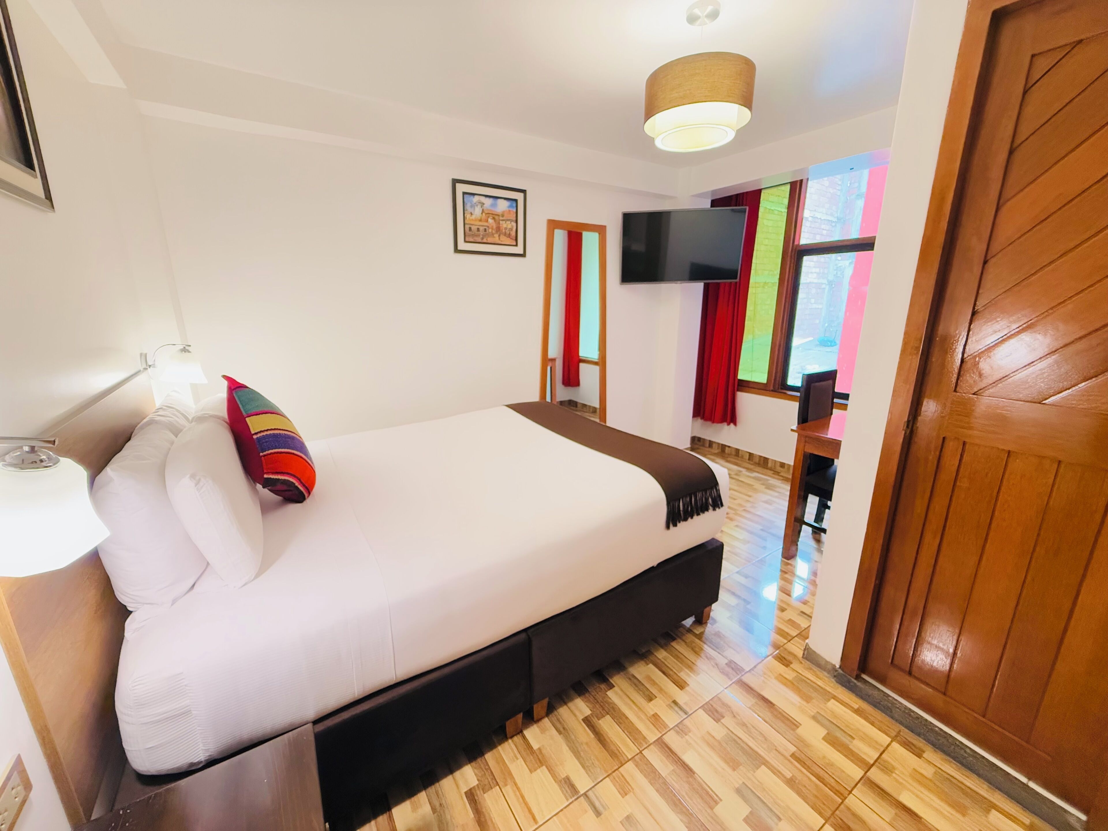 Quarto de hotel com cama, escrivaninha, televisão e janela com cortinas.