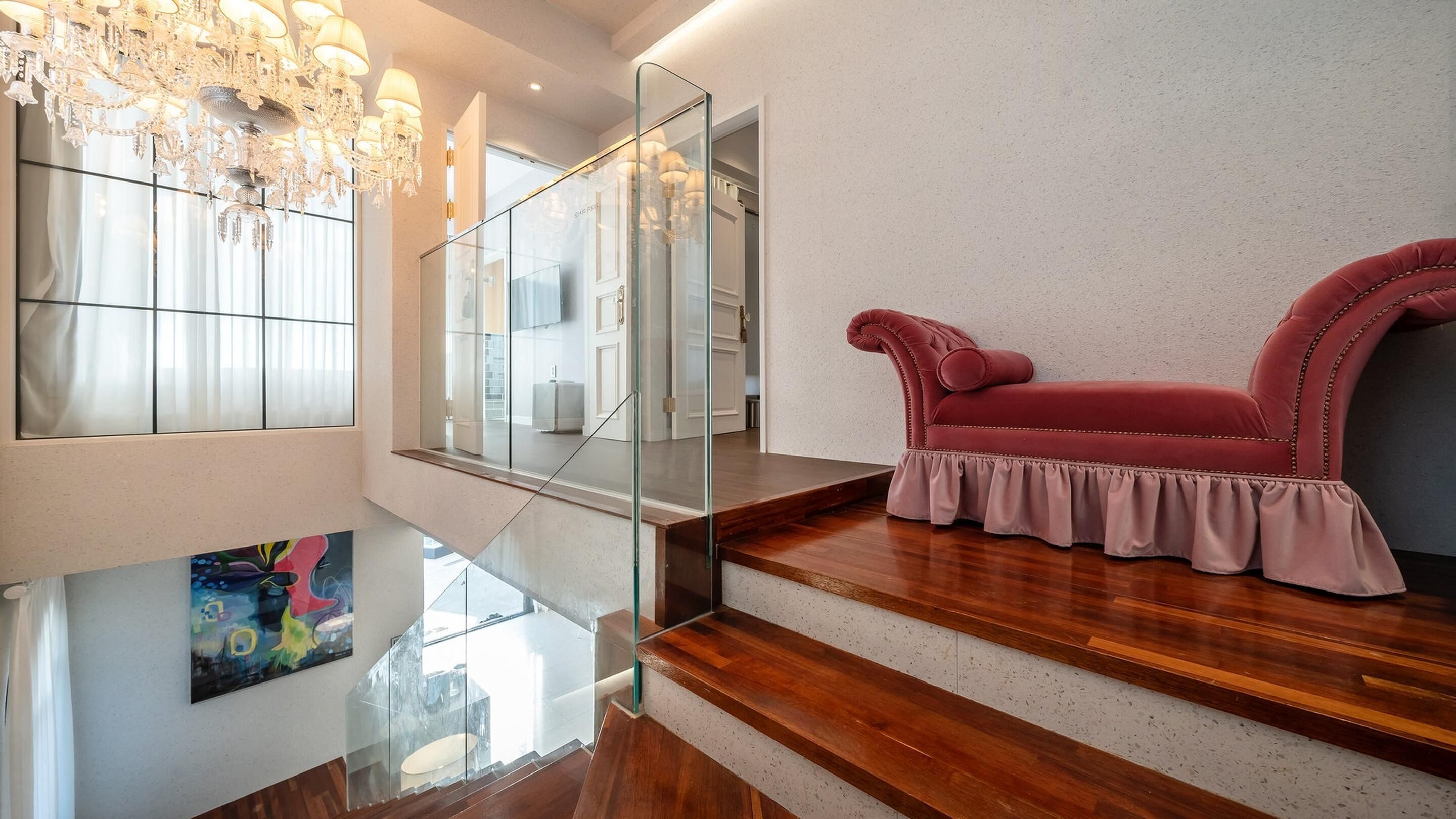 Um interior moderno com escada de madeira, guarda-corrimão de vidro e poltrona estofada vermelha.