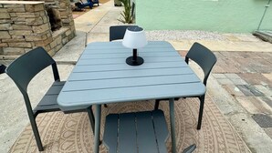 Mesa externa quadrada com uma luminária solar, cercada por quatro cadeiras.