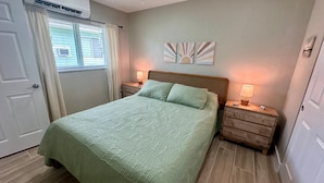 Quarto com cama, duas mesas de cabeceira com abajures, janela com cortinas e uma parede com três quadros de raios de sol.