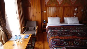 Quarto de madeira com cama, cadeira, mesa e garrafas de água, e parede com padrão.
