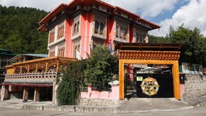 Edifício tradicional com fachada vermelha e janelas ornamentadas, apresentando um portão de entrada de madeira com um emblema colorido.
