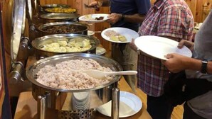 Buffet montado com diversos alimentos em grandes recipientes de metal.