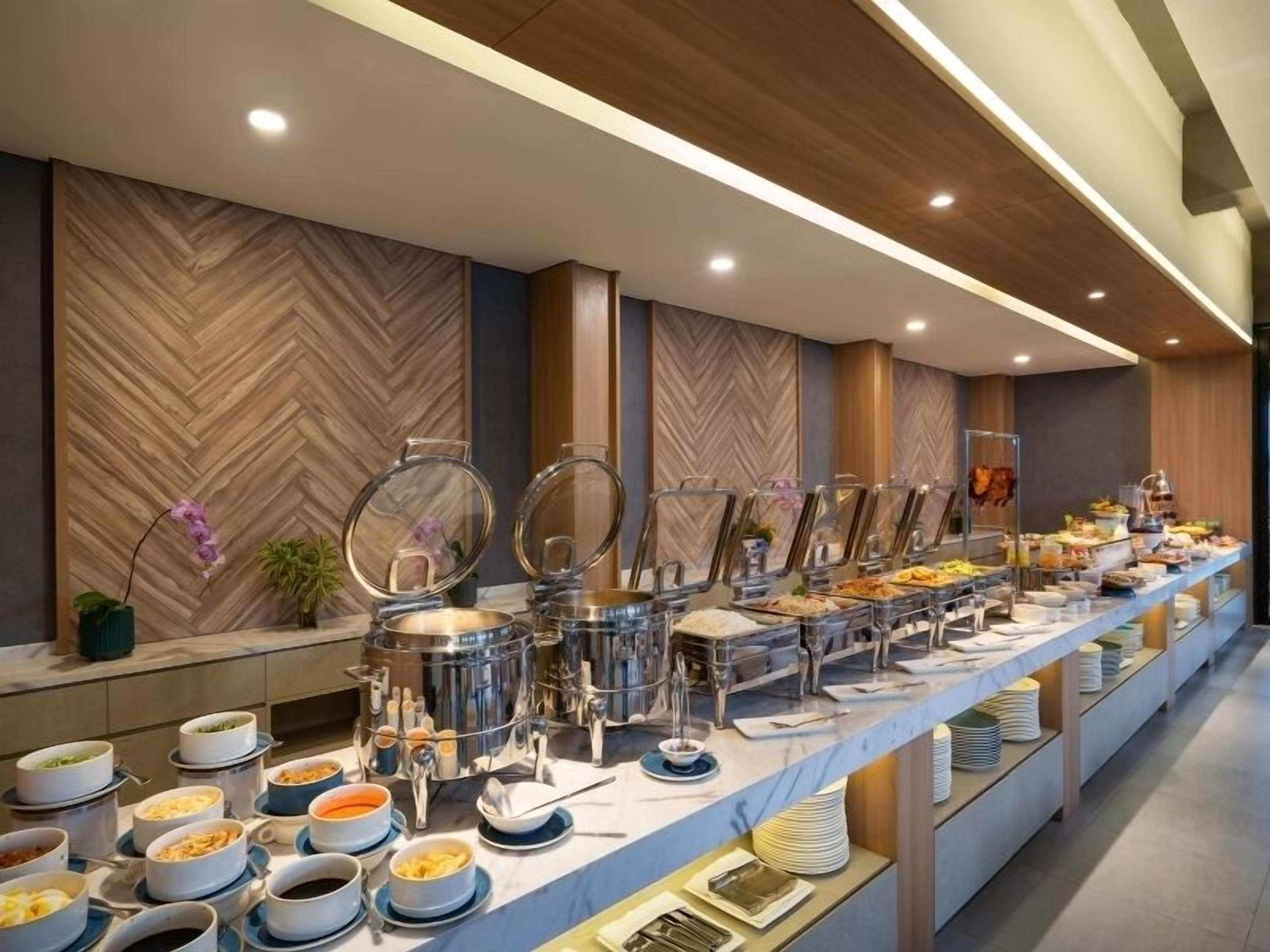 Disposição de buffet com várias estações de serviço, incluindo recipientes e repondedores para alimentos, dispostos sobre uma mesa longa.