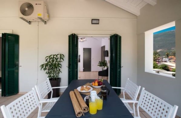 Uma área de refeições ao ar livre coberta, com uma mesa posta para dois, um ventilador e vista para a cidade.