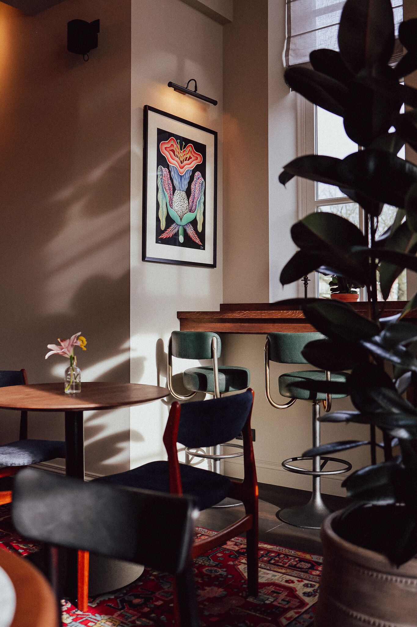 Quarto com mesa de jantar, cadeiras, uma obra de arte emoldurada na parede, um vaso de planta e uma janela com vista.