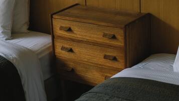 Uma cômoda de madeira com três gavetas, uma cama com lençol branco e uma cabeceira de madeira.