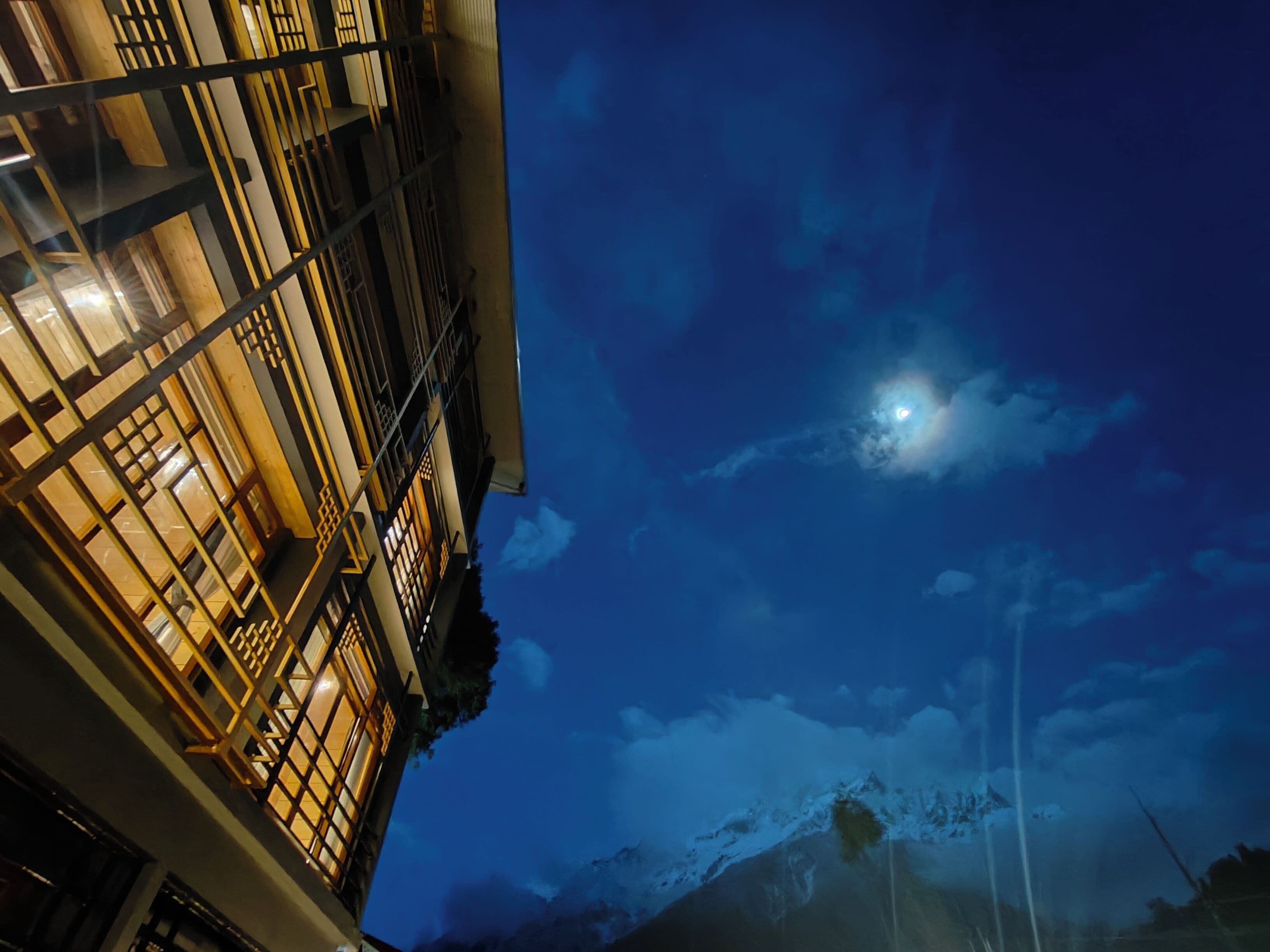 Um edifício com estilo arquitetônico tradicional, apresentando janelas com treliças de madeira e uma lua visível no céu noturno.