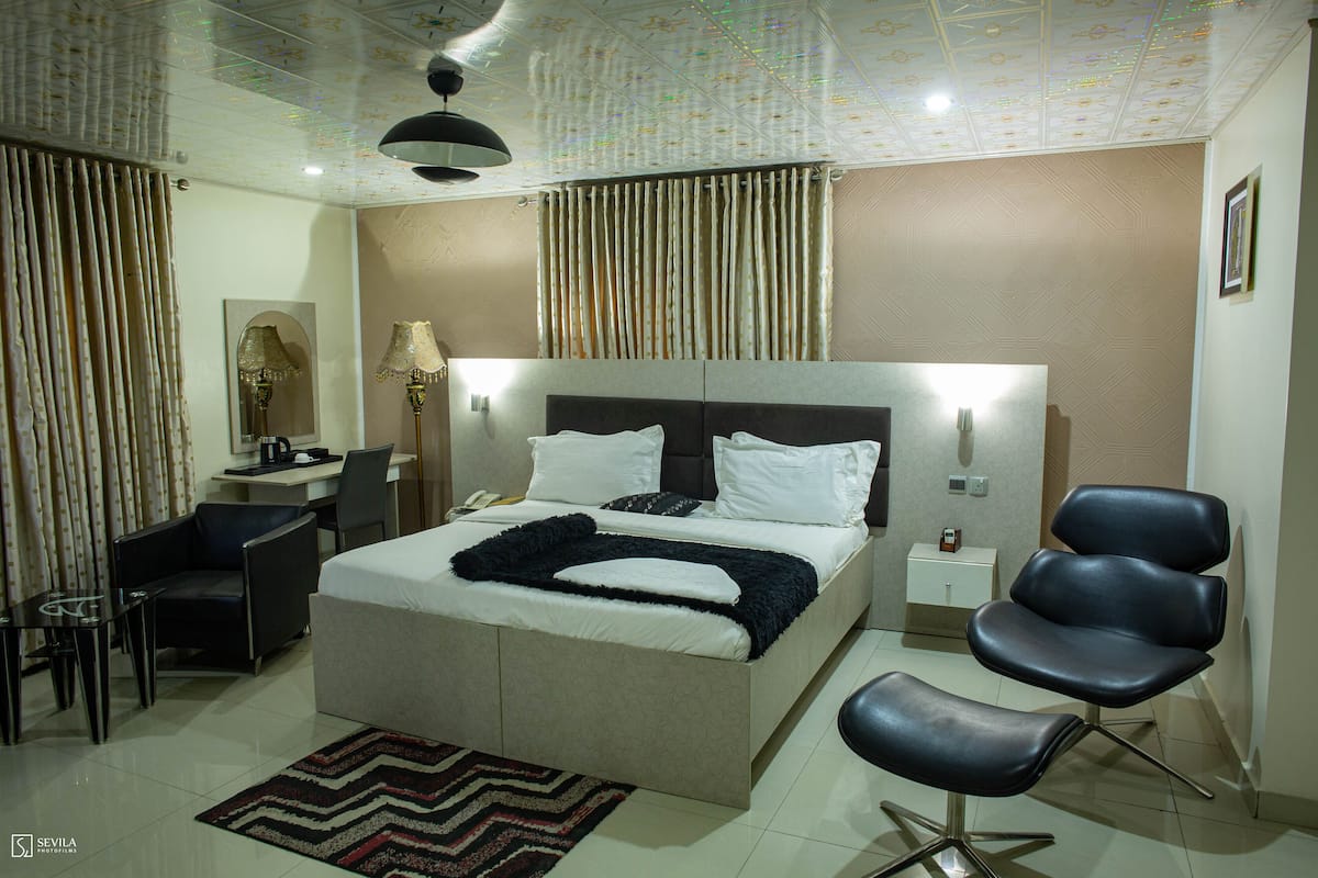 Quarto de hotel moderno com uma cama grande, uma escrivaninha, uma cadeira e uma mesinha.