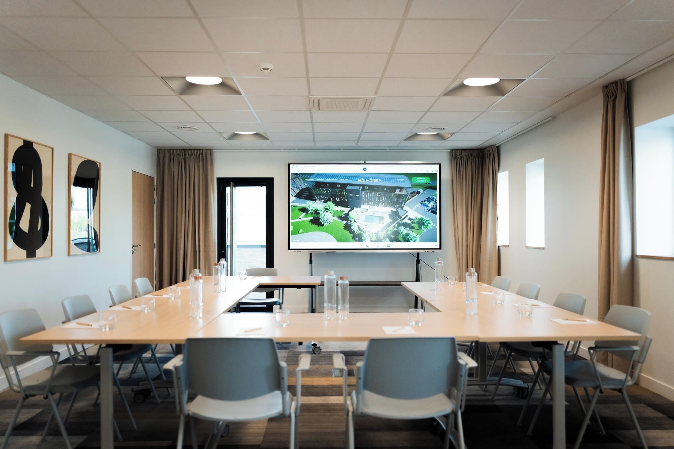 Uma sala de conferência com uma mesa comprida, cadeiras, uma tela de projetor e uma janela grande.