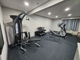 Academia com equipamentos de ginástica, incluindo um banco prensa, halteres e uma máquina elíptica.