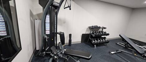Uma academia com um banco de musculação, halteres e um aparelho de polia.