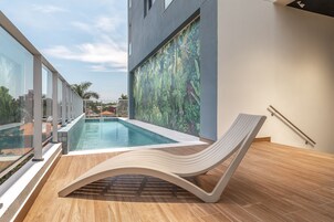 Uma área de piscina moderna com guarda-corpo de vidro, uma espreguiçadeira e um mural de folhagem tropical na parede adjacente.