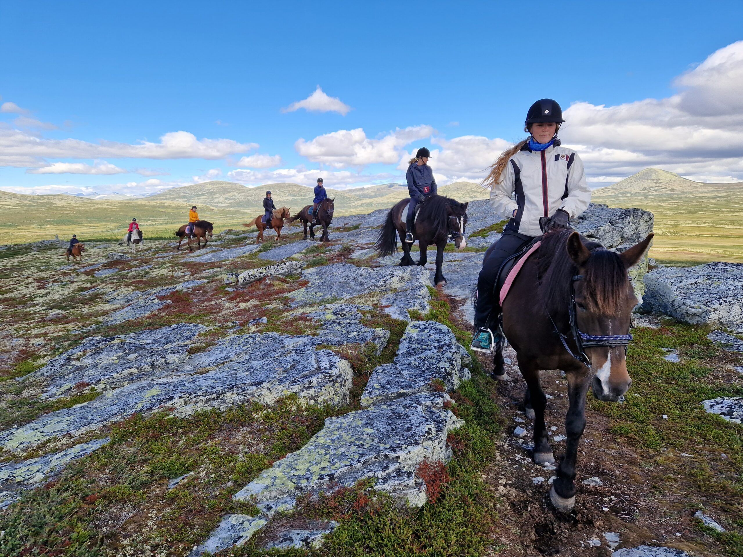 Um grupo de pessoas a cavalo em terreno rochoso, com montanhas ao fundo.