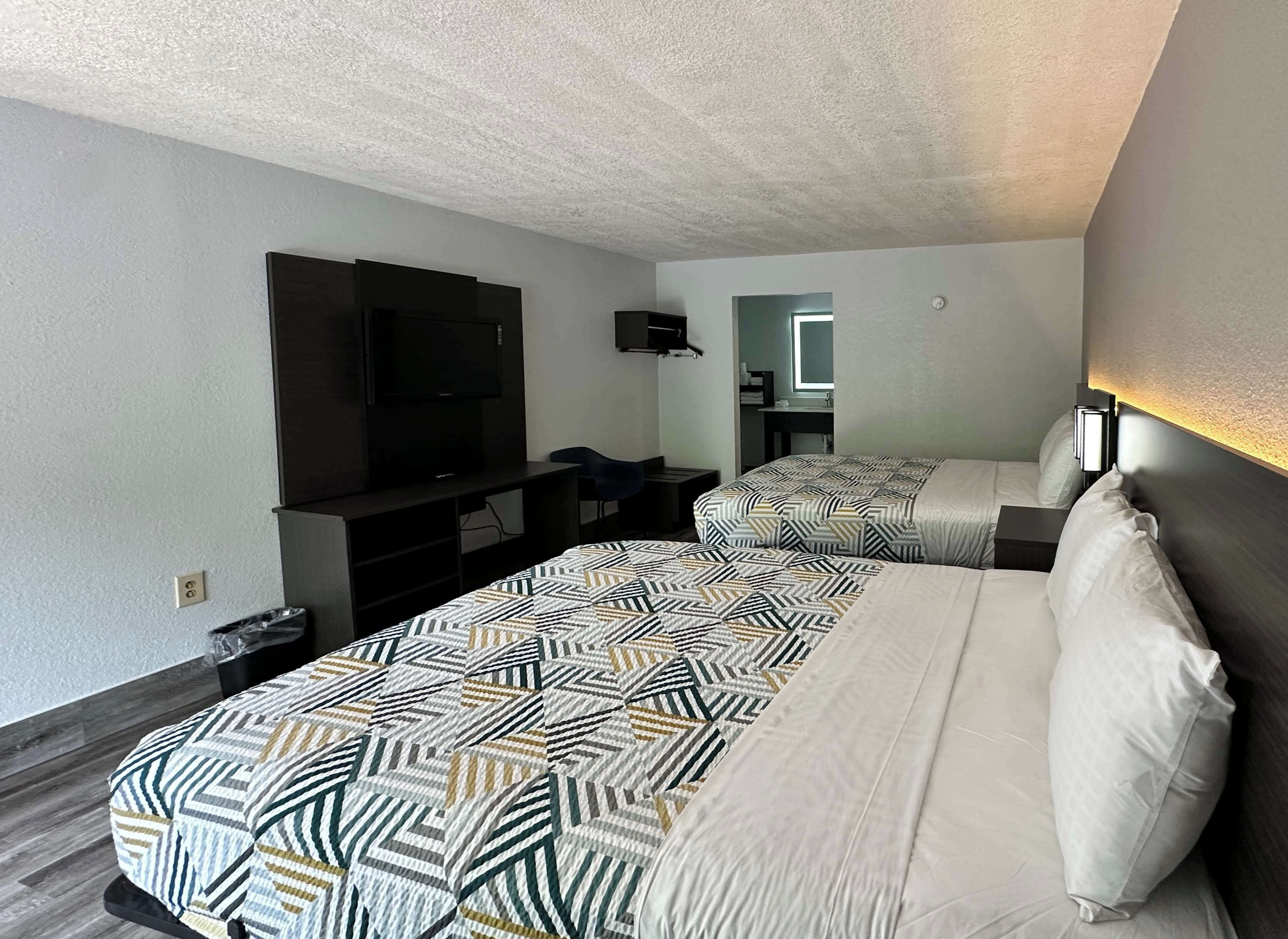 Quarto de hotel com duas camas, televisão, escrivaninha e espelho.