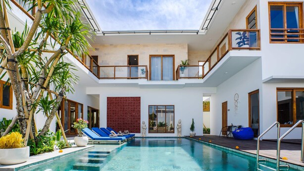 Um hotel moderno com piscina central, várias varandas e plantas tropicais.