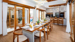 Uma sala de jantar com uma longa mesa de madeira posta para seis pessoas, rodeada por cadeiras de madeira.