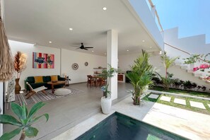 Uma sala de estar moderna com sofá, mesa de centro e área de refeições. Há uma piscina em primeiro plano.
