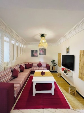 Uma sala de estar com sofá, mesa de centro, televisão e luminária decorativa suspensa.