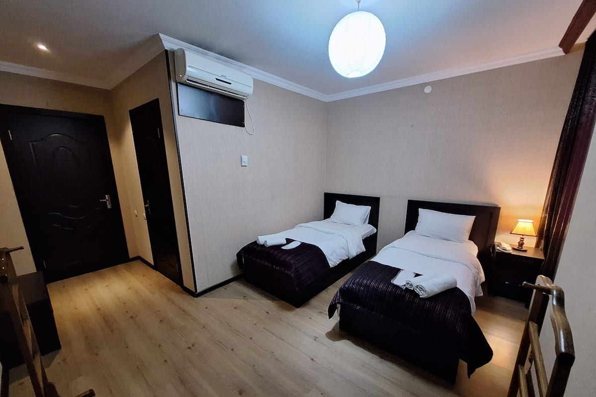 Quarto de hotel com duas camas, uma escrivaninha, ar condicionado e uma luminária.
