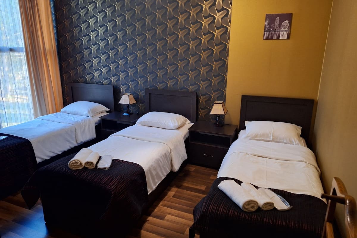 Quarto de hotel com duas camas de solteiro, mesa de cabeceira com abajur, piso de madeira e parede estampada.