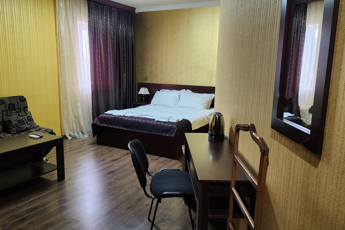 Quarto de hotel com cama, escrivaninha, cadeira, sofá e espelho.