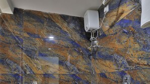 Uma casa de banho com parede de mármore, sanita, chuveiro e um porta-toalhas.