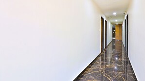 Um corredor comprido e estreito, com paredes brancas e chão de mármore preto.