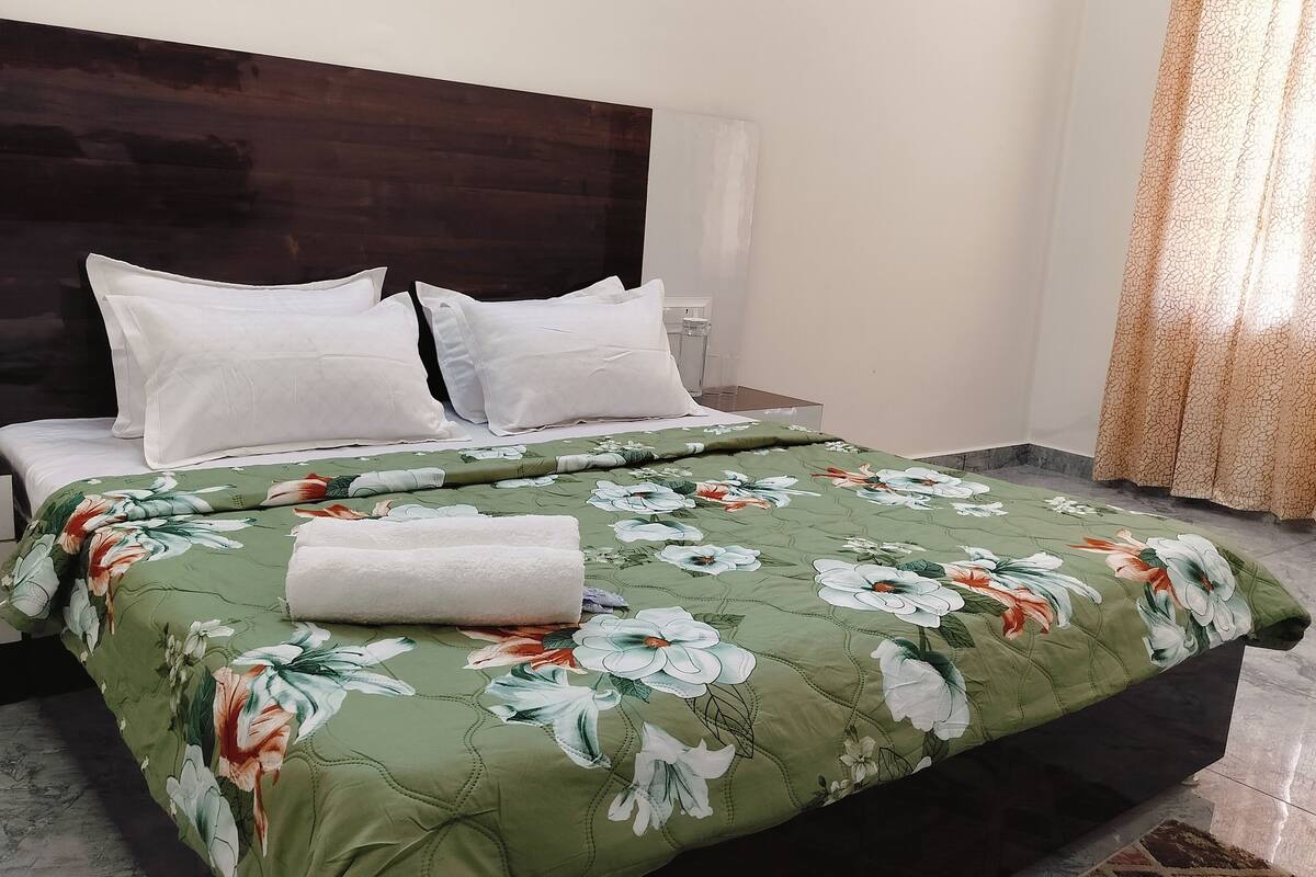 Cama bem arrumada com colcha florida, travesseiros brancos e toalha dobrada.