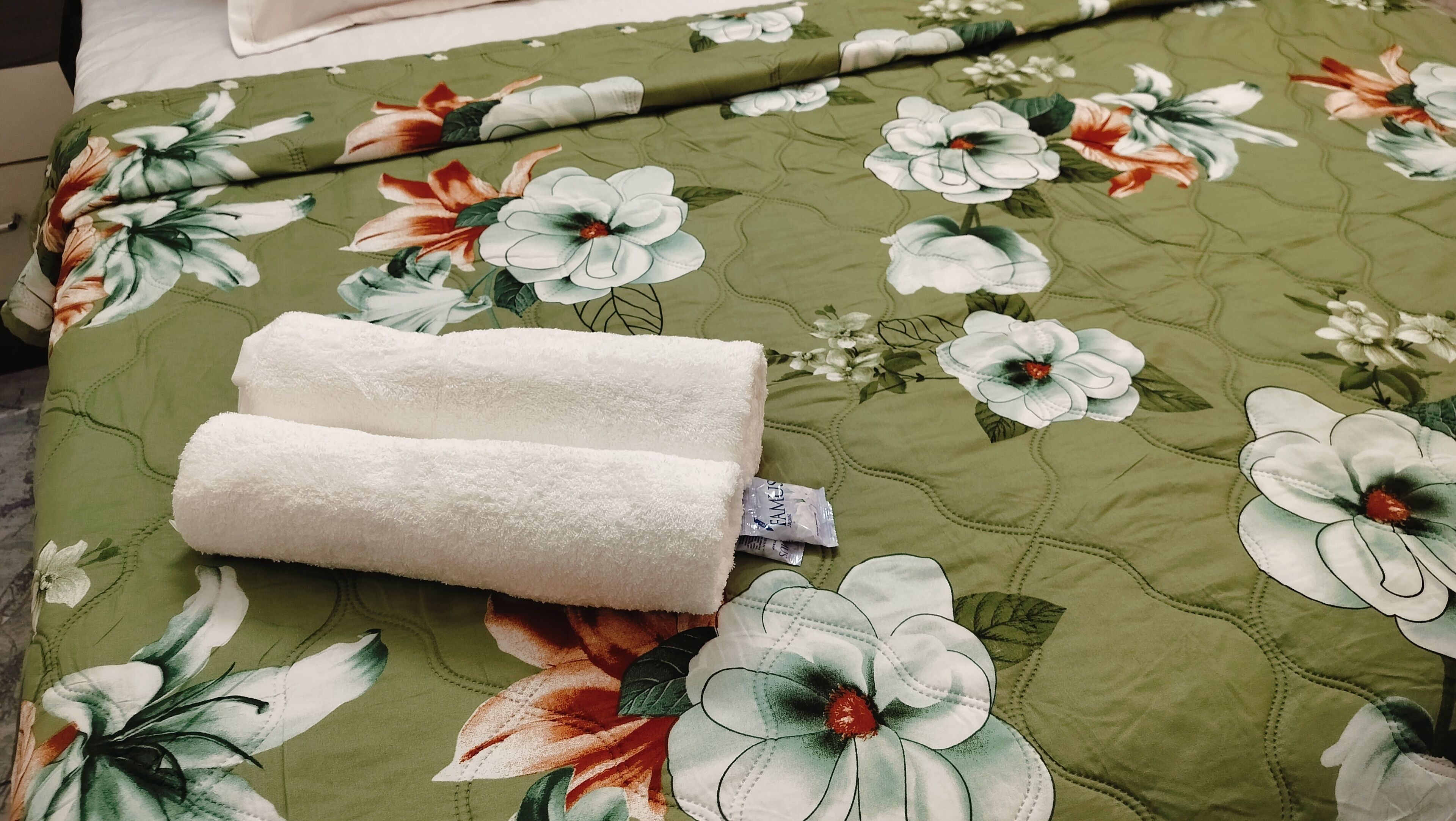 Uma cama com colcha floral verde e duas toalhas brancas dobradas com cuidado.