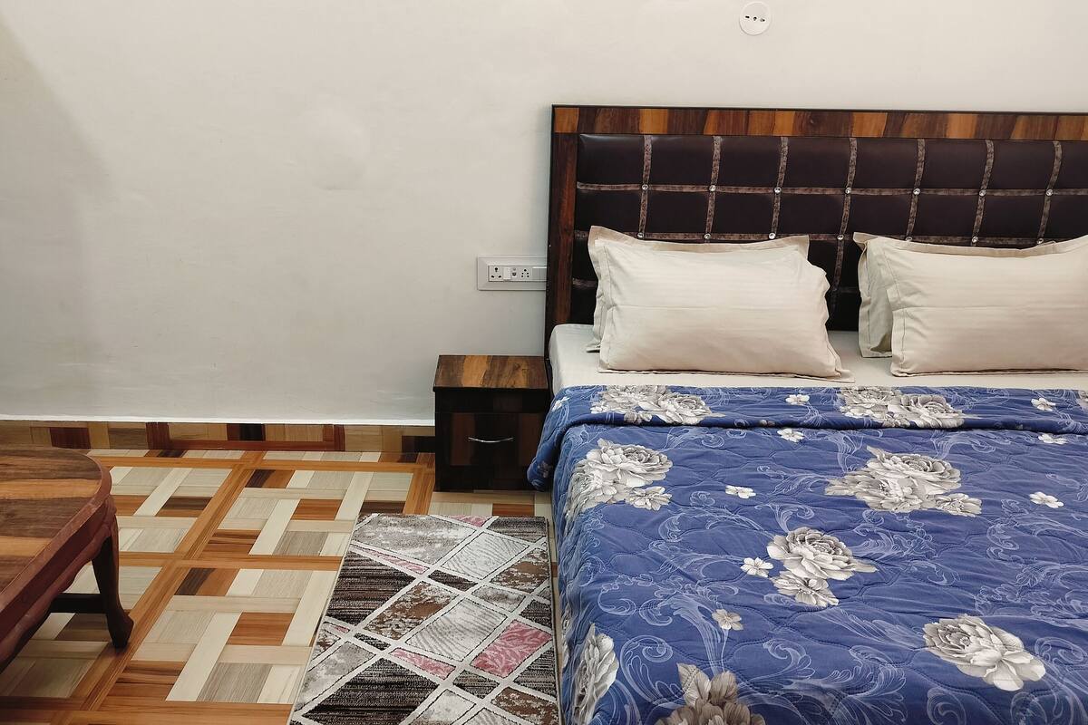 Quarto com cabeceira de madeira, cama com colcha florida, mesa de cabeceira e tapete estampado.