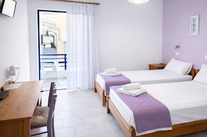Quarto de hotel com duas camas de solteiro, uma escrivaninha de madeira, uma cadeira e uma pequena mesa com luminária.